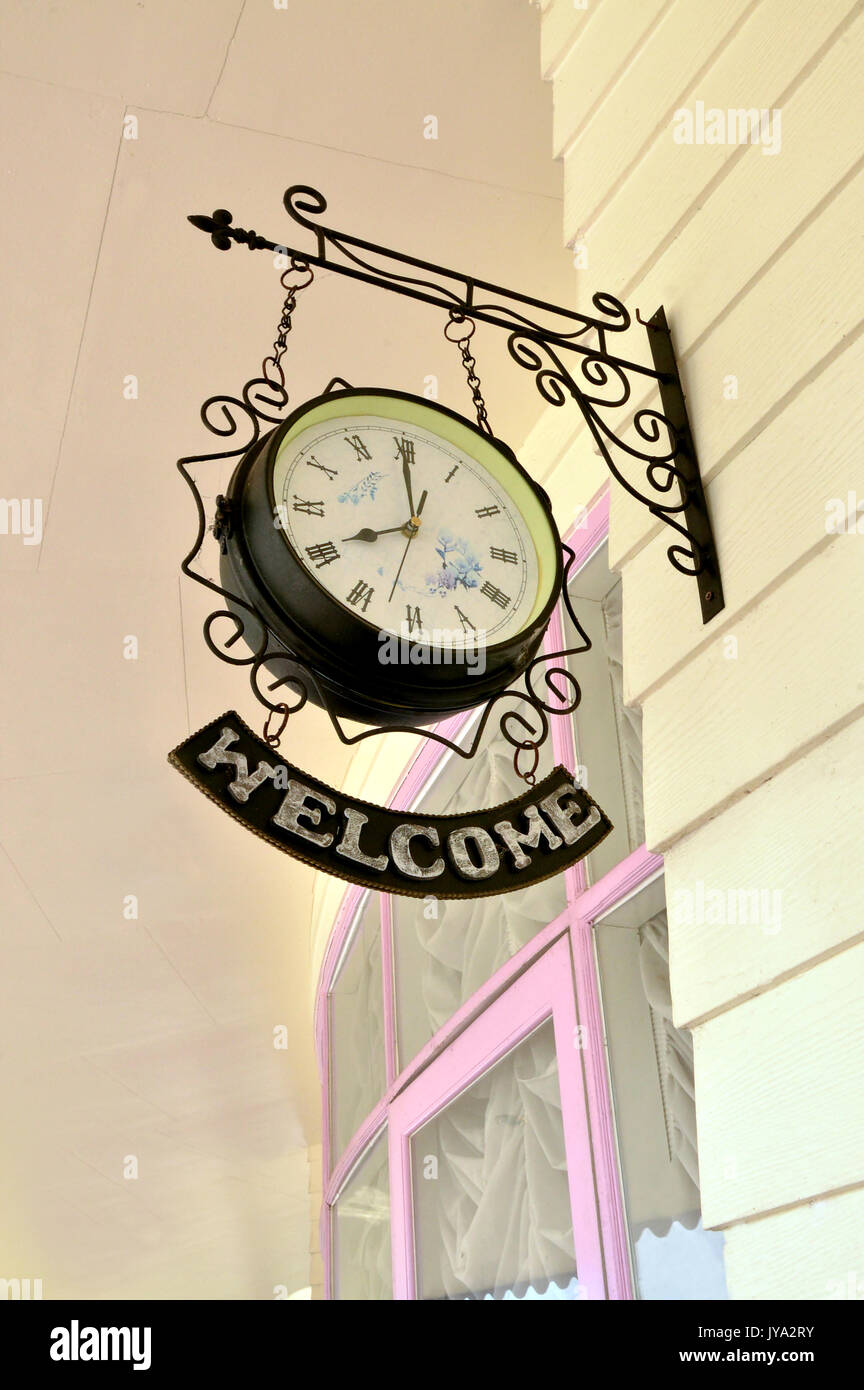 Vintage style clock hanging. With signs welcoming Stock Photo - Alamy