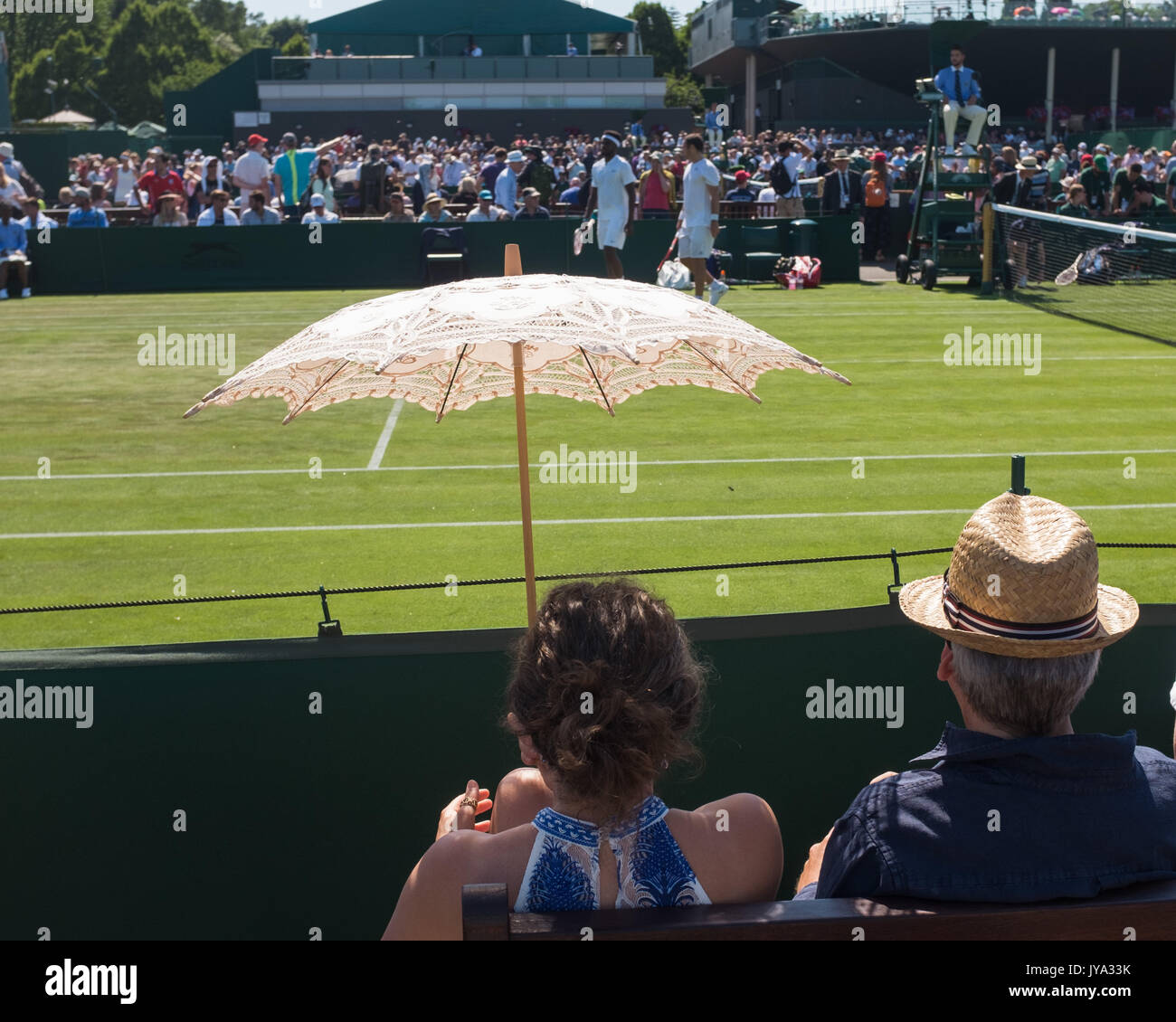 Spectators sitting on bench with umbrella on outside court at Wimbledon ...