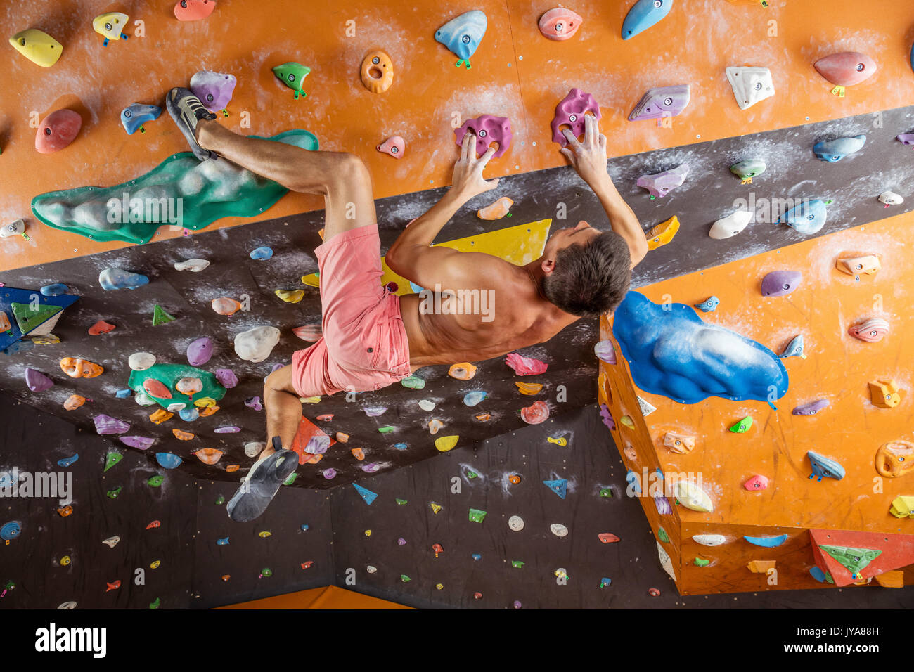 Young man bouldering in indoor climbing gym, trying to solve ...