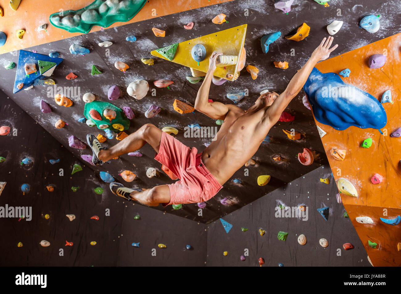 Young man bouldering in indoor climbing gym, trying to reach next ...