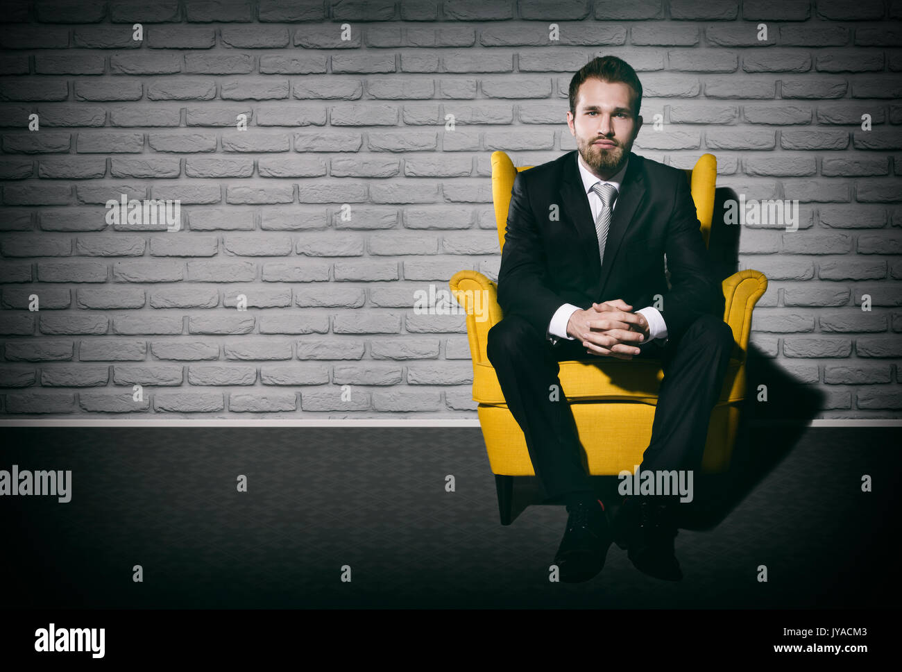 Handsome businessman sitting alone on armchair in empty room ...