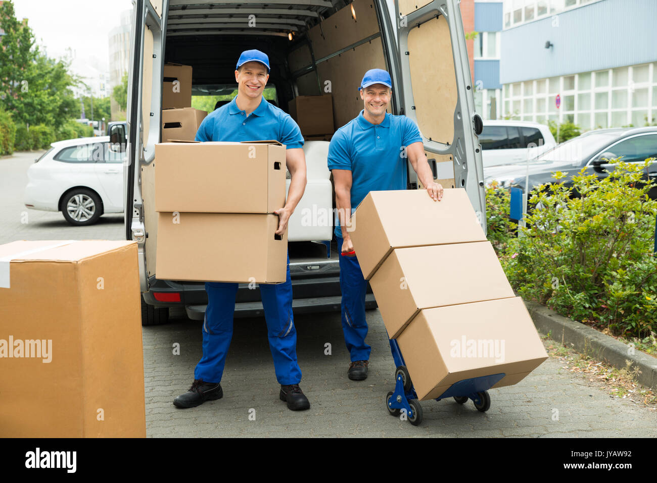 Two Happy Male Workers Loading Stack Of Cardboard Boxes In Truck Stock ...