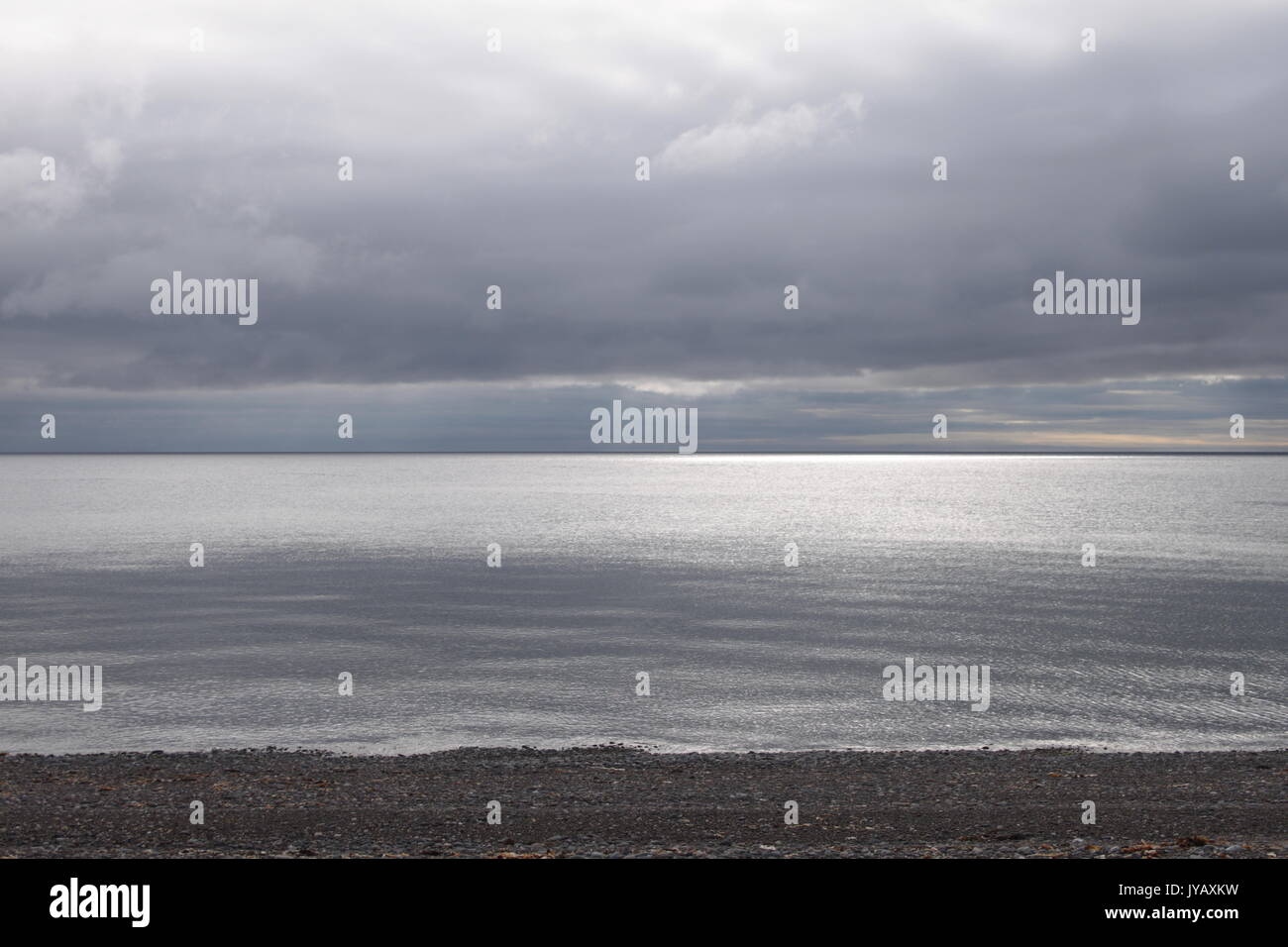 Grey beach leads to a grey sea or ocean under a grey sky on a grey day ...