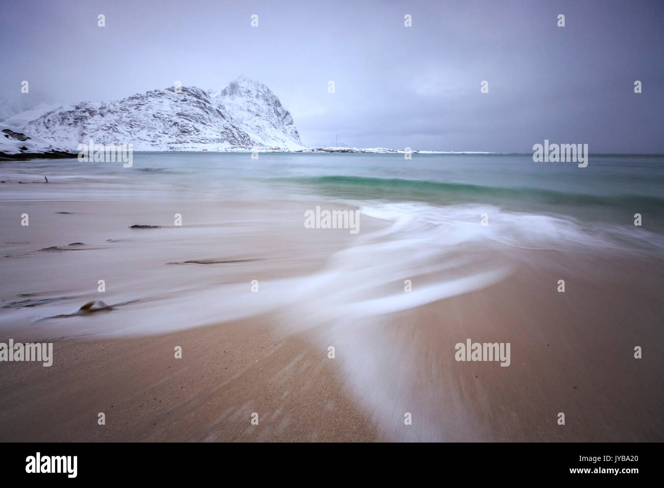 Waves of the icy sea on the beach in the background the snowy peaks ...