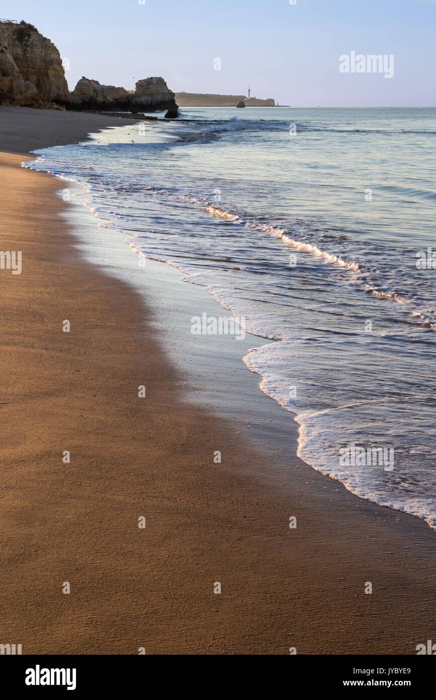 The rising sun illuminates the fine sand bathed by the blue ocean Praia ...
