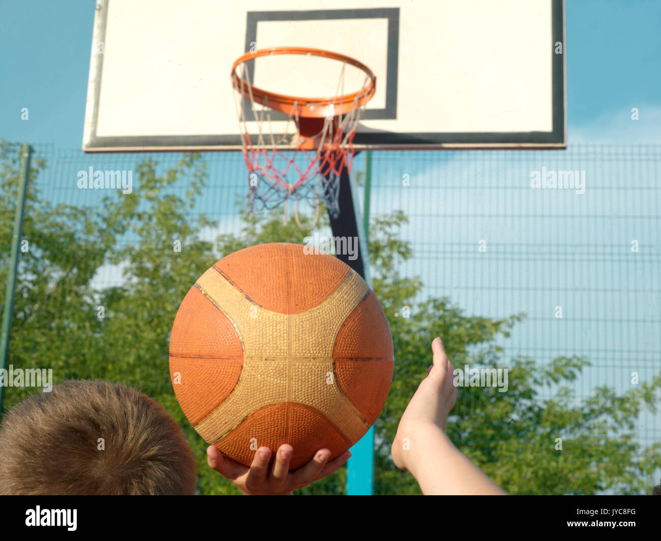 Children throwing a ball into the basket, playing basketball outdoors ...
