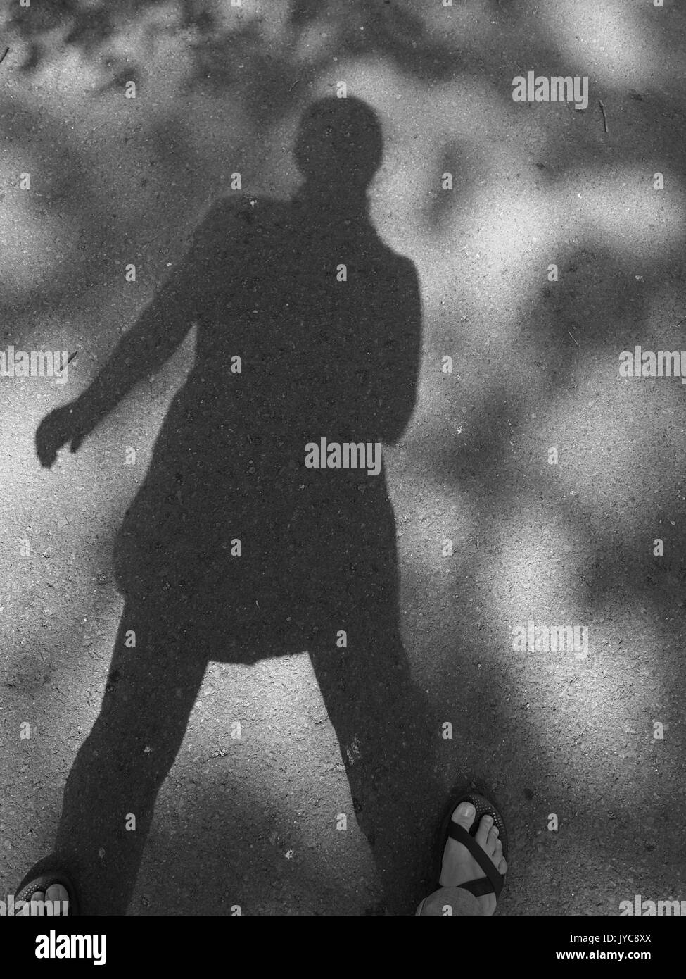 Shadow cast by a woman extending from her feet, under the dappled light ...
