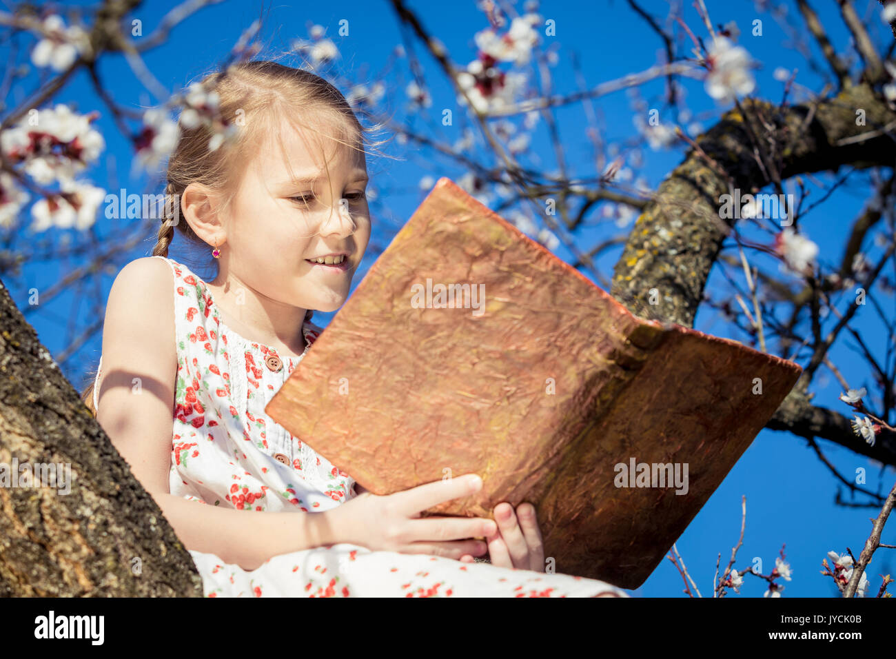 One little girl reading a book on a blossom tree. Concept children and ...