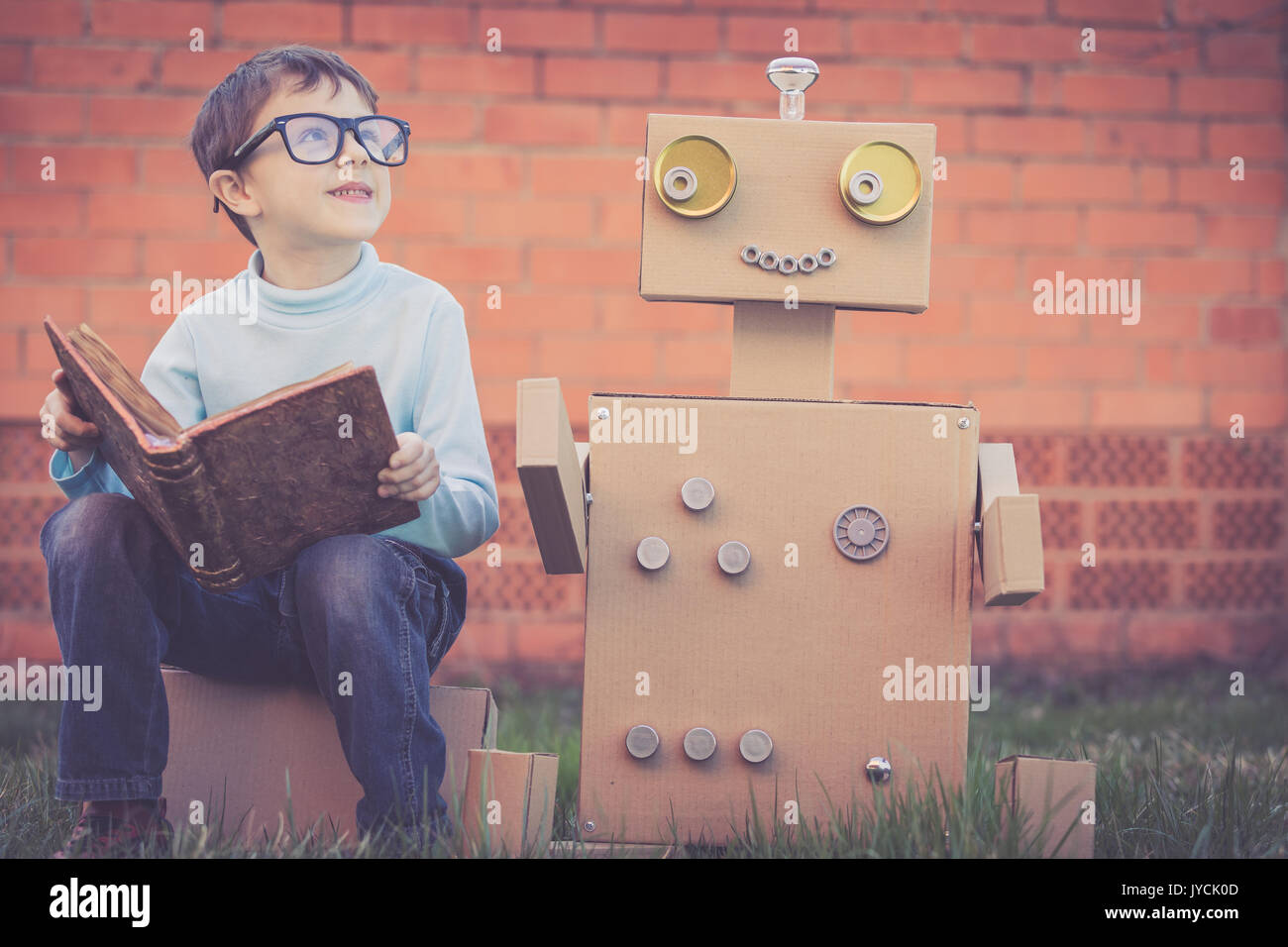 One little boy reading to robot from cardboard boxes outdoors. Concept ...