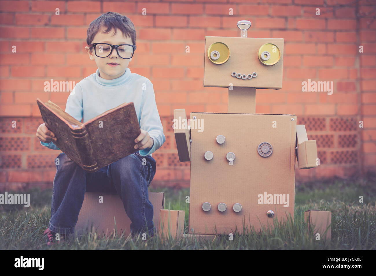 One little boy reading to robot from cardboard boxes outdoors. Concept ...