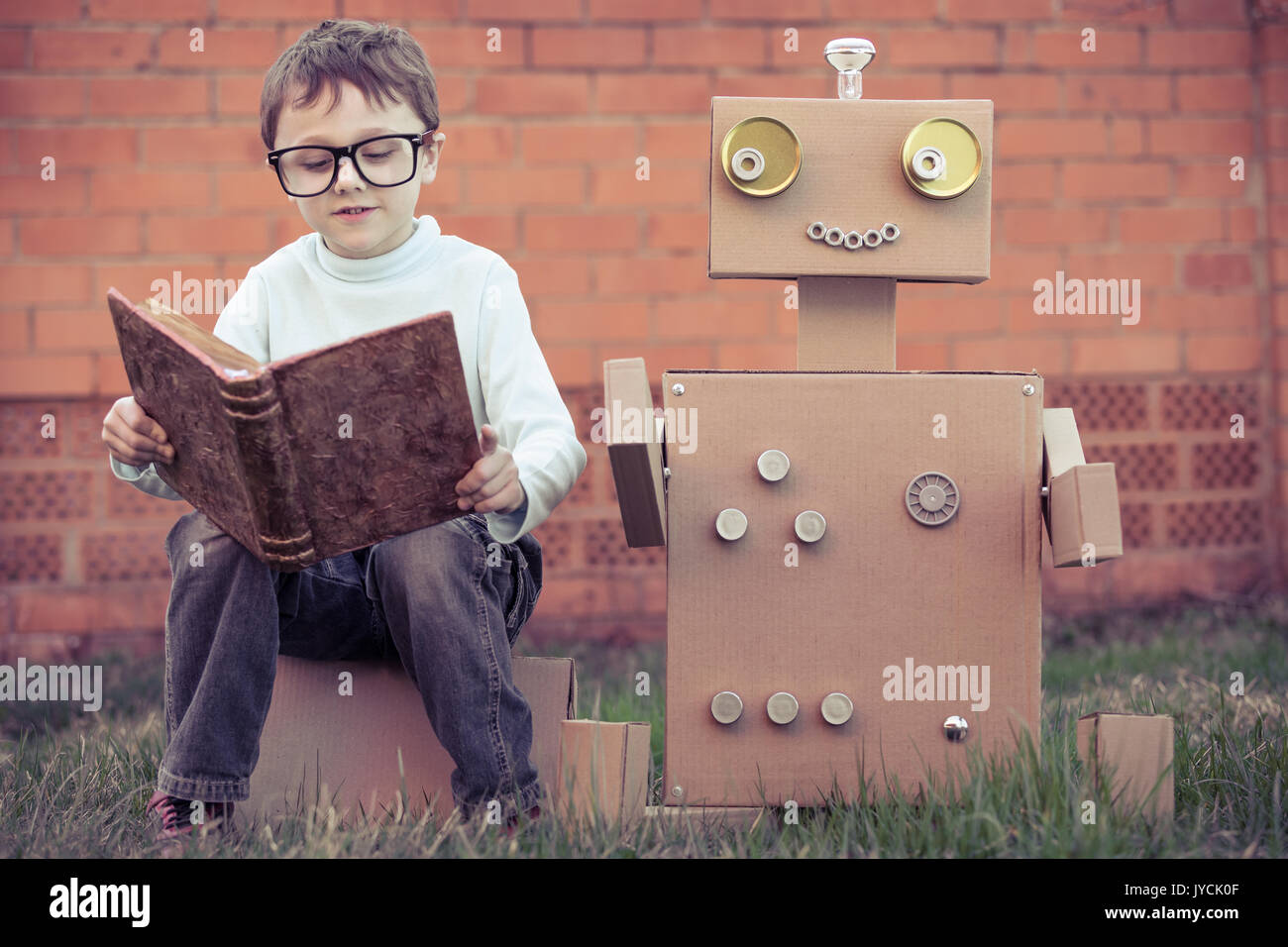 One little boy reading to robot from cardboard boxes outdoors. Concept ...