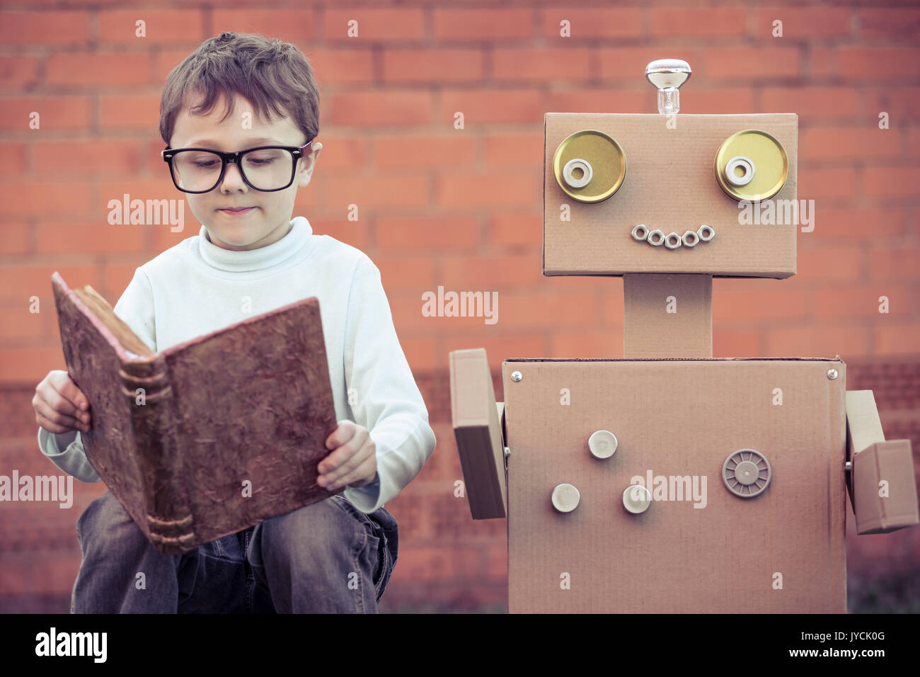 One little boy reading to robot from cardboard boxes outdoors. Concept ...