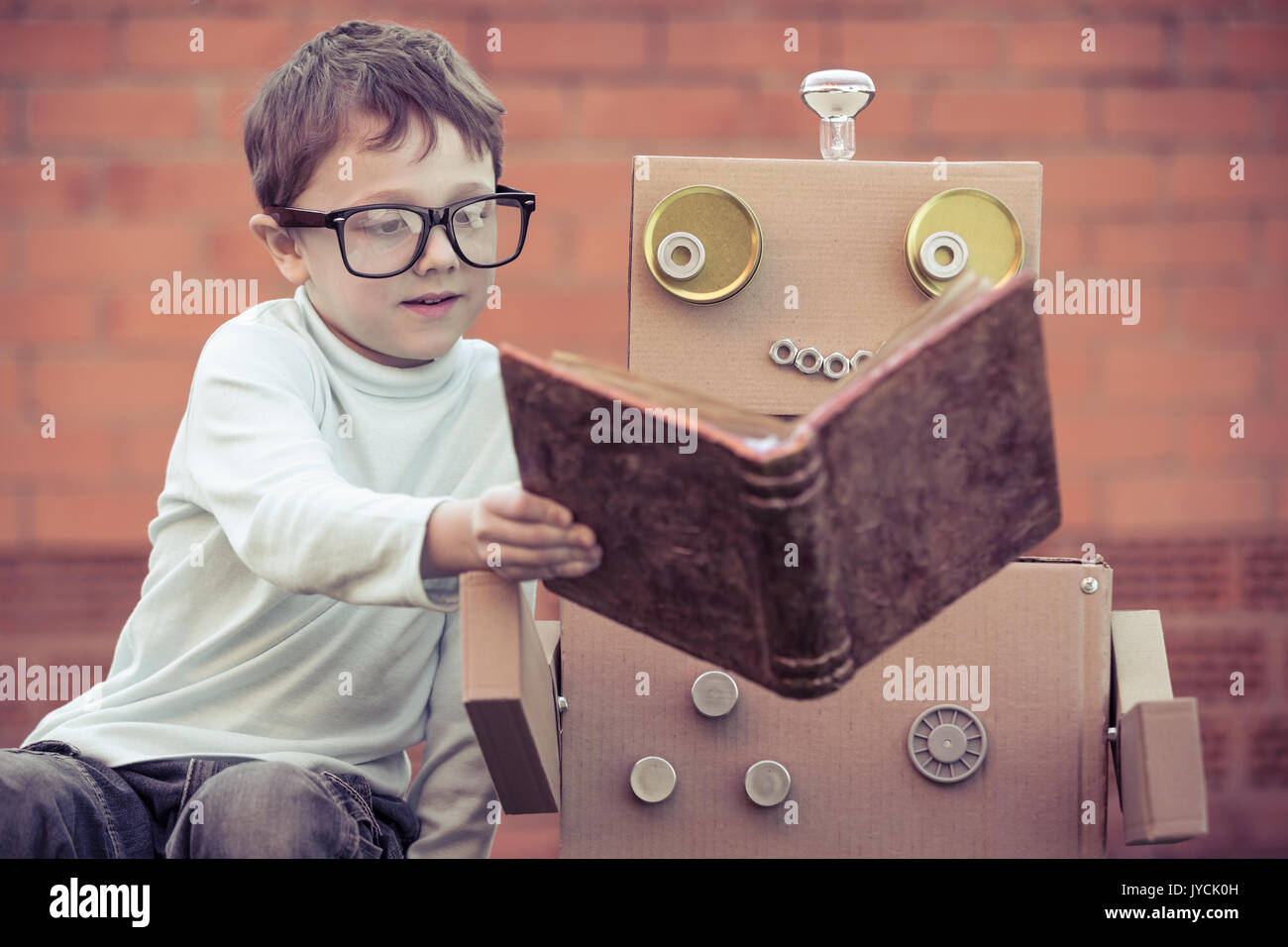 One little boy reading to robot from cardboard boxes outdoors. Concept ...