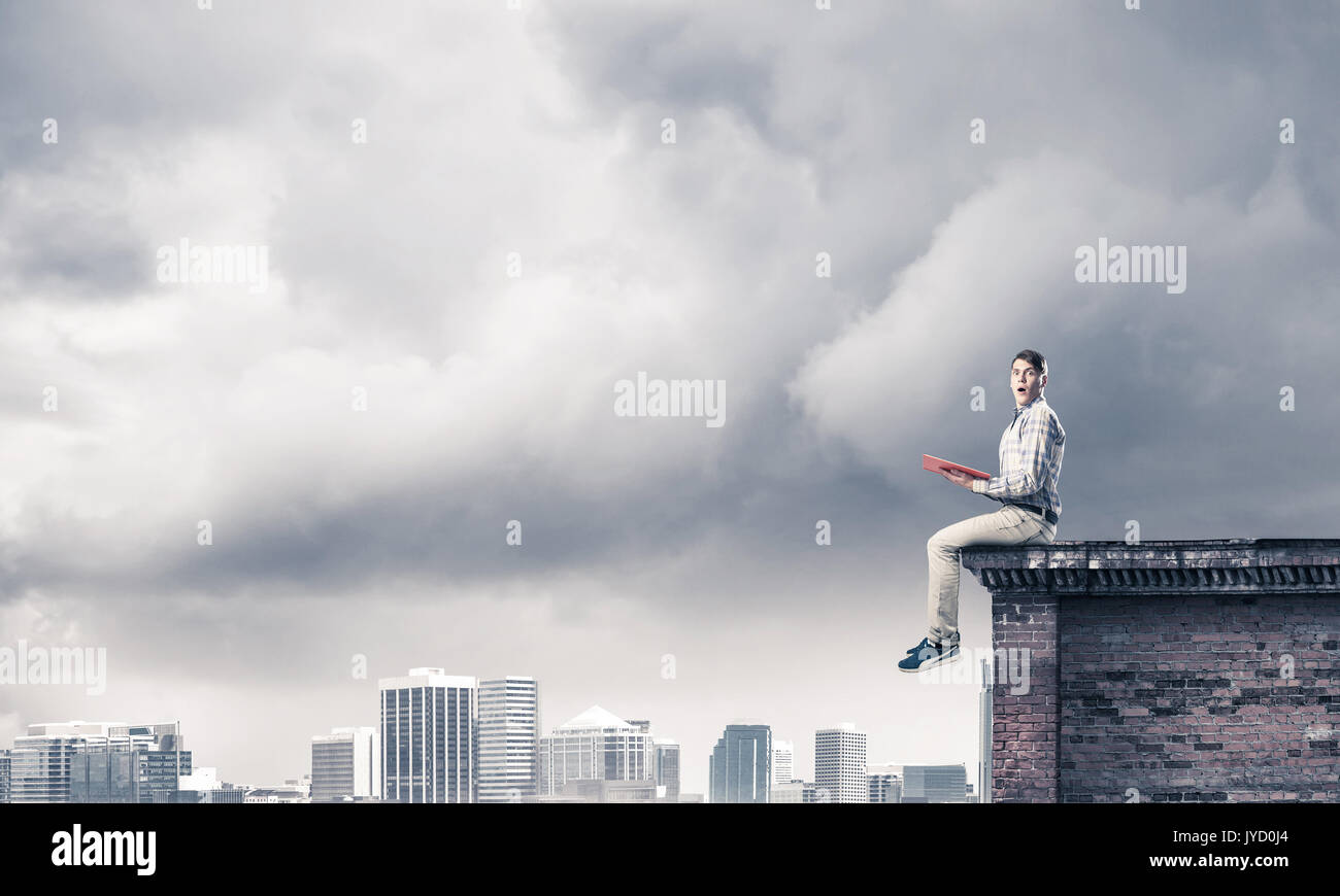 Man on roof edge reading book and cityscape at background Stock Photo ...