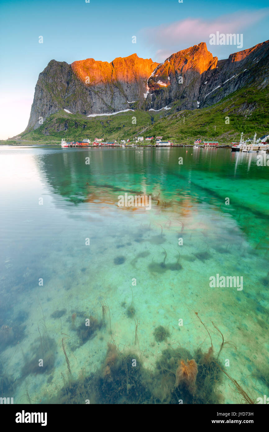 Midnight sun on fishing village surrounded by clear sea and peaks Reine ...
