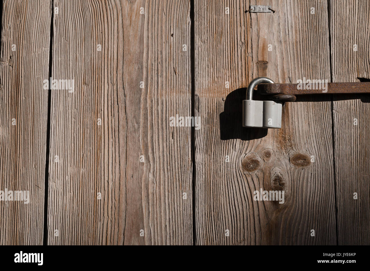 The new iron lock on an old metal fixing hangs on a high wooden gate, a ...