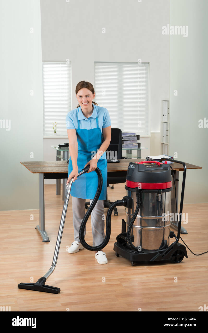 Happy Female Worker Cleaning Floor With Vacuum Cleaner In Office Stock ...