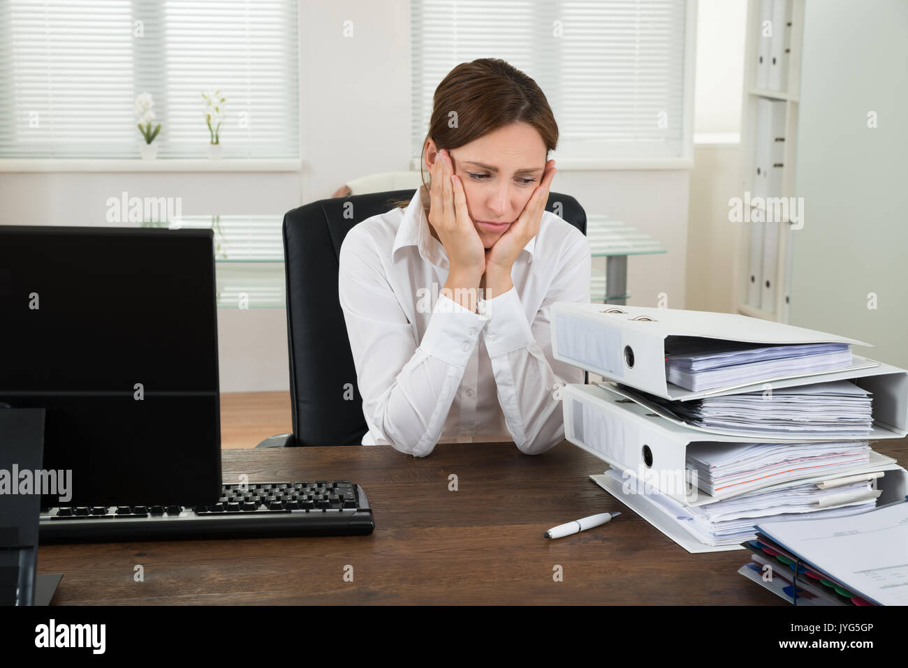 Stressed Young Businesswoman Looking At Stack Of Folders In Office ... Stressed Young Businesswoman Looking At Stack Of Folders In Office ...
