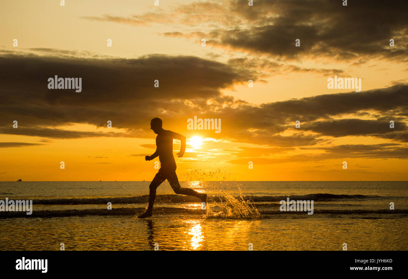 Jogger running in the sea at sunrise during UK heatwave Stock Photo - Alamy