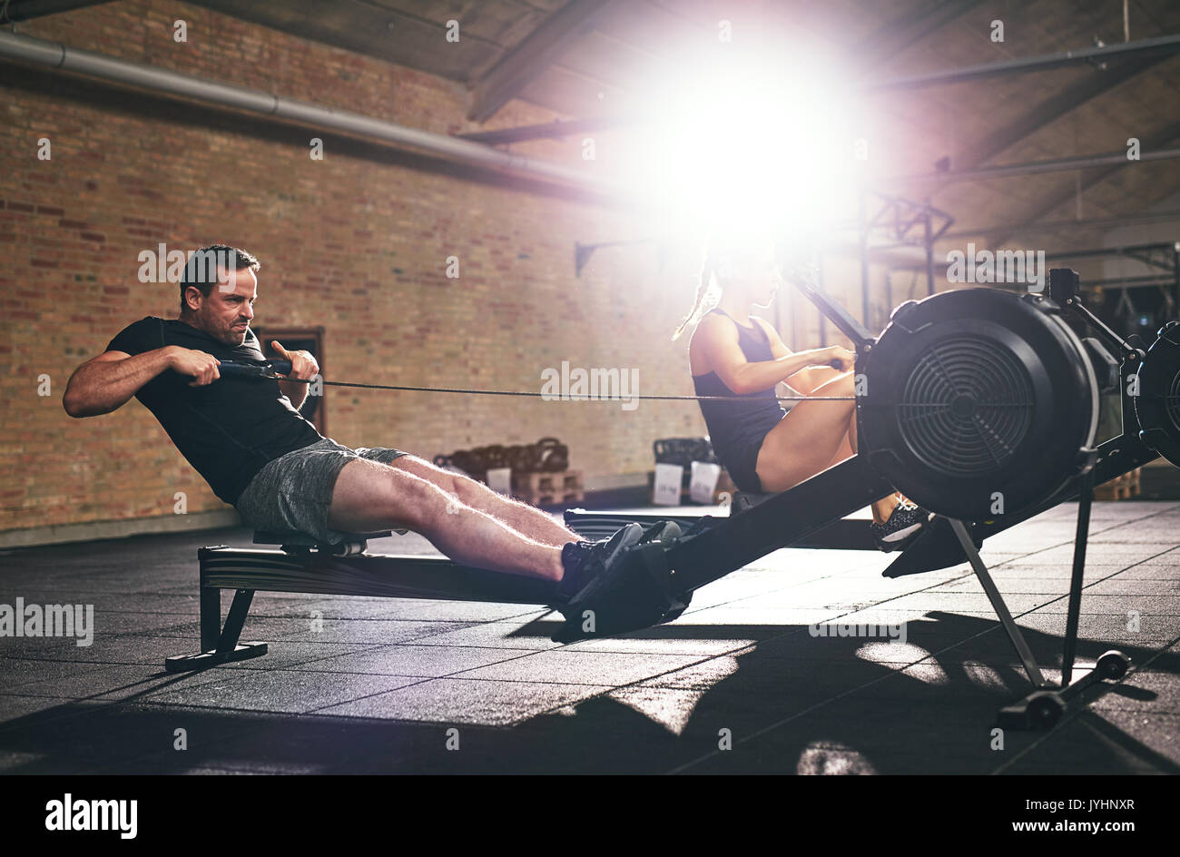 Two young sportsmen having hard workout on rowing machines in light gym ...