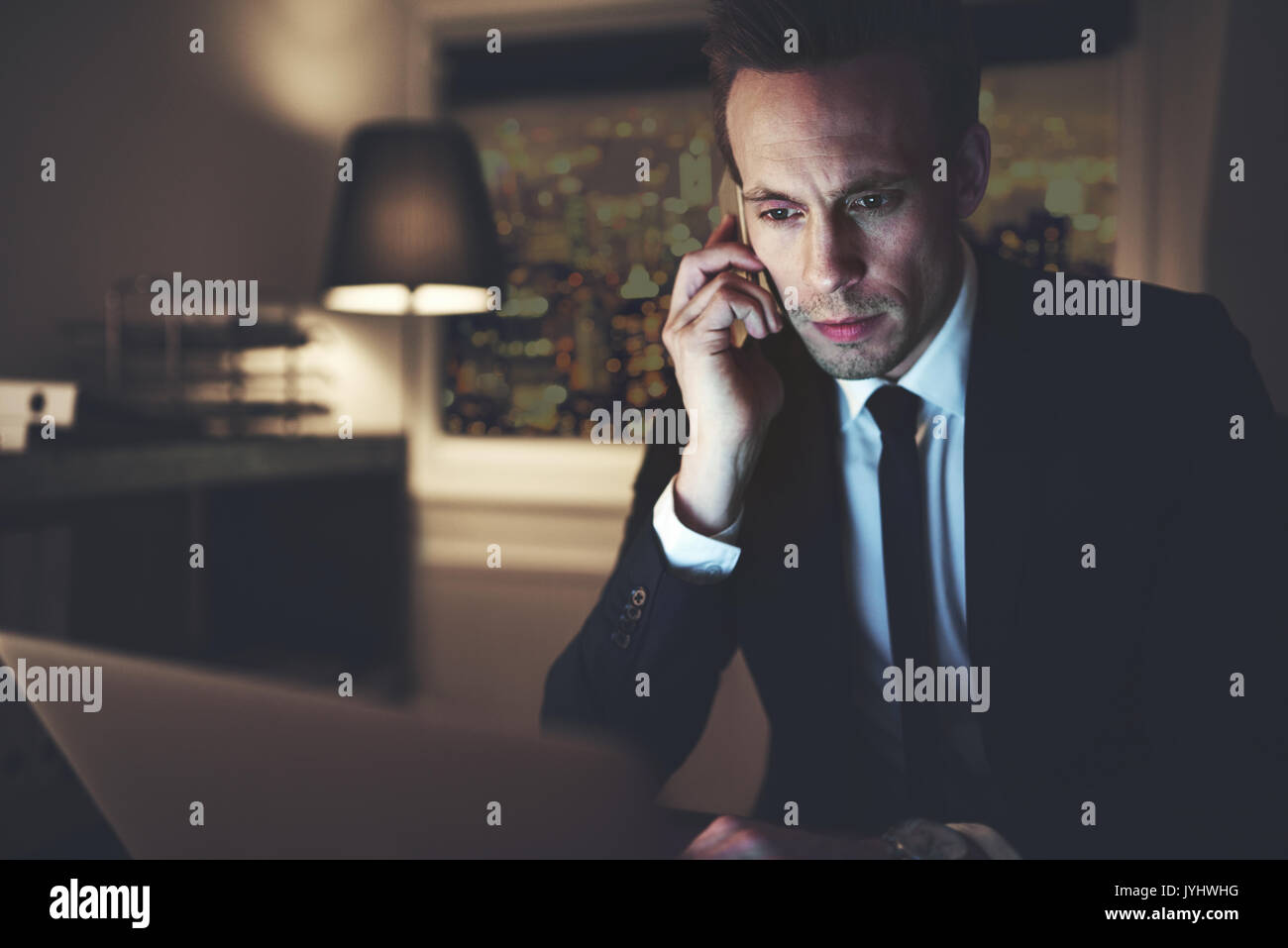 The office worker sitting at the laptop and talking the smartphone in ...