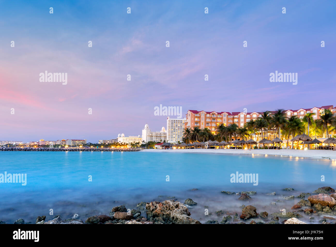 High Rise hotel area in Aruba at dusk. Palm trees in motion suggest the ...
