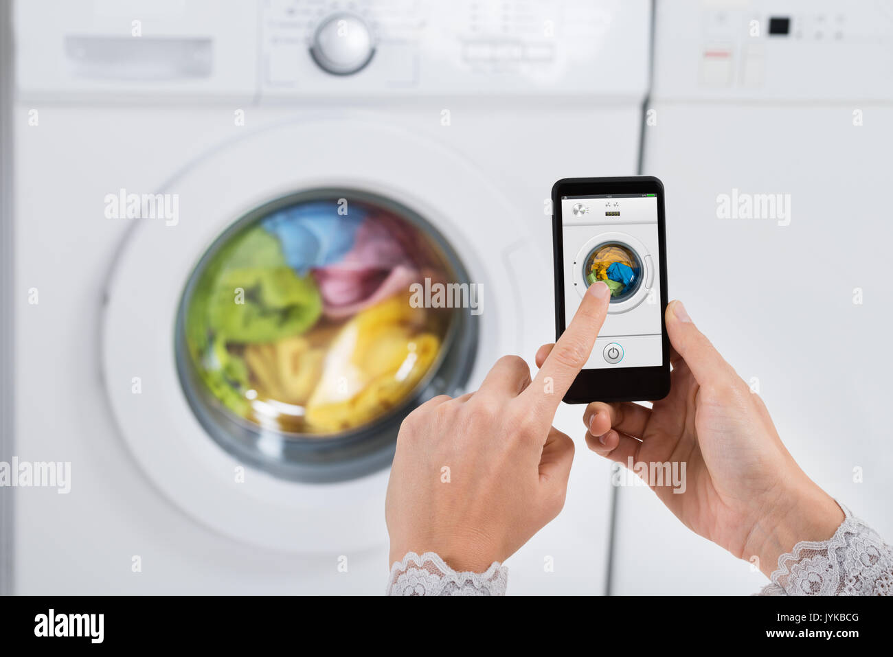 Close-up Of Person Hands Operating Washing Machine With Mobile Phone ...