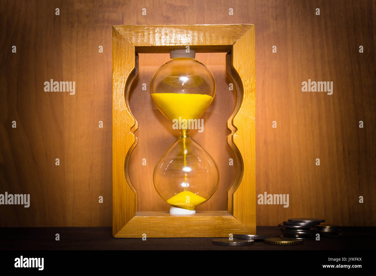 The glossy old-style hourglass standing with a coins Stock Photo - Alamy