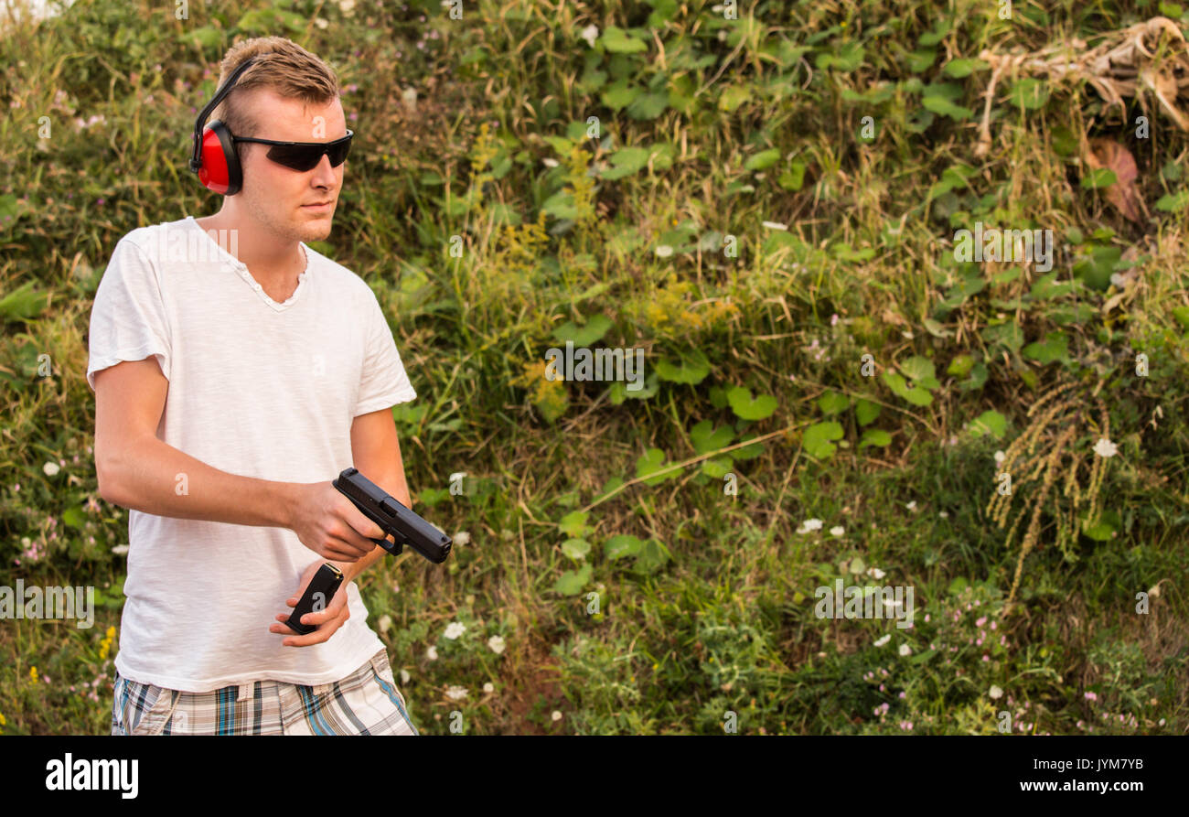 Blonde caucasian handsome guy with gun glock pistol changing magazine ...