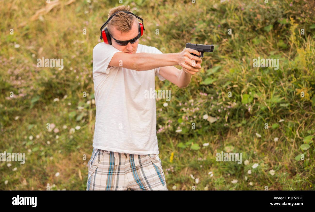 Young and strong caucasian blond guy firing bullets at the enemy target ...