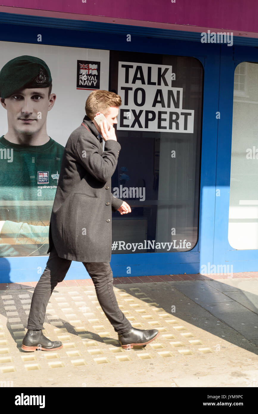 Man walking past a Royal Navy recruitment office whilst talking on a ...