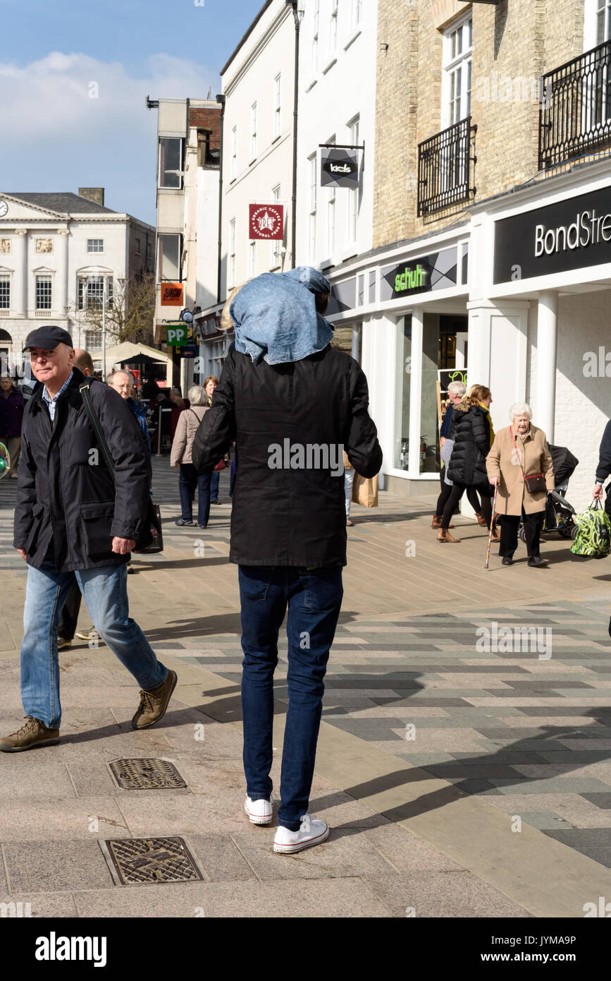 Tall man walking down a high street in England carrying a child on his ...