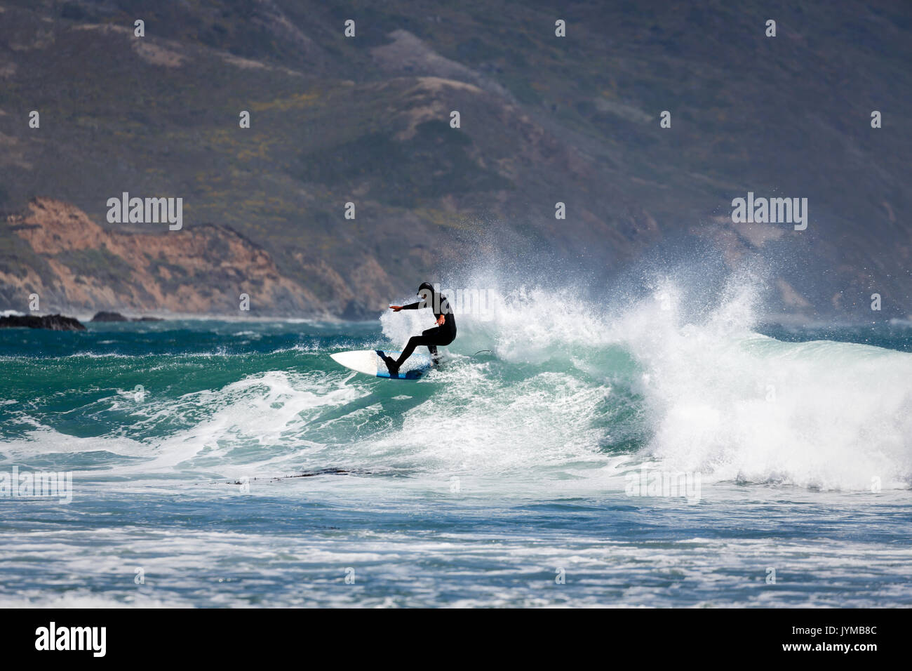 Cold water surfer in black wetsuit cuts a sharp turn on top of wave ...