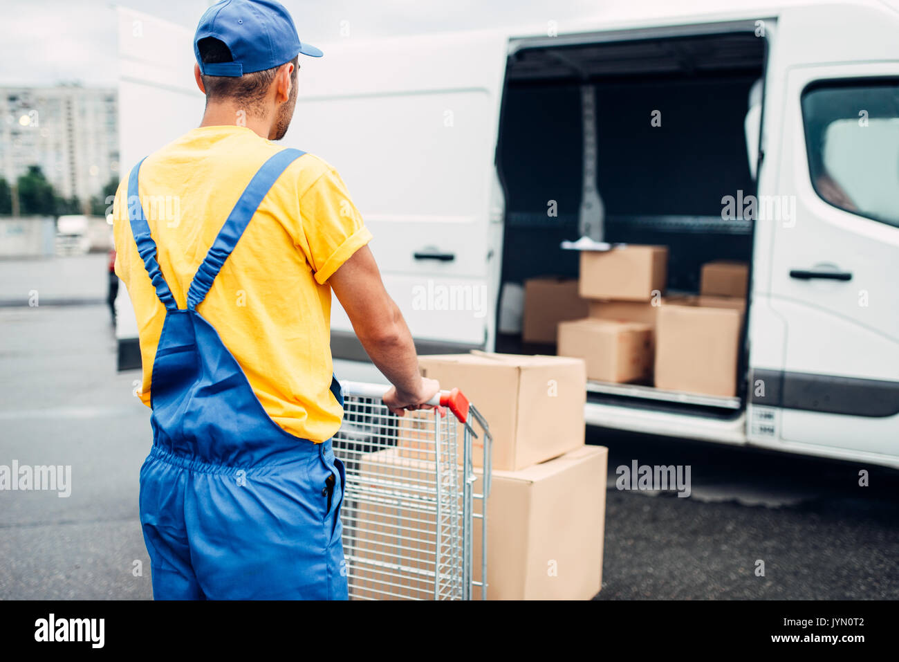 Male courier in uniform works with cargo, back view. Truck with parcels ...