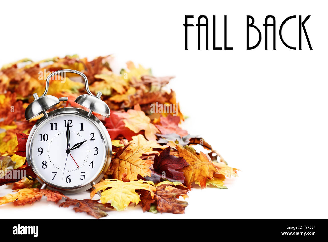 Alarm clock in colorful autumn leaves isolated against a white ...