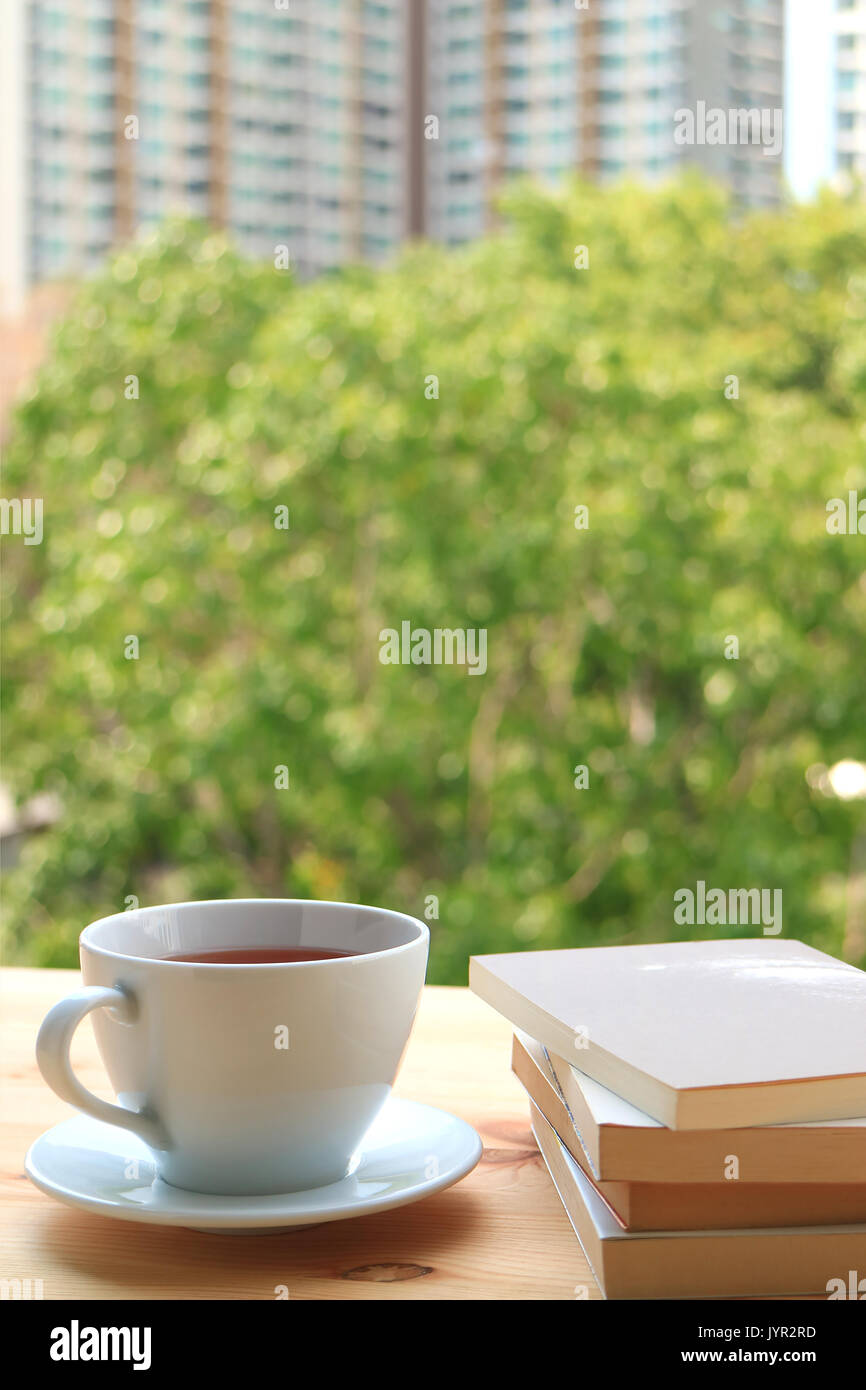 Cup of hot tea with stack of books on wooden table by the window, with ...