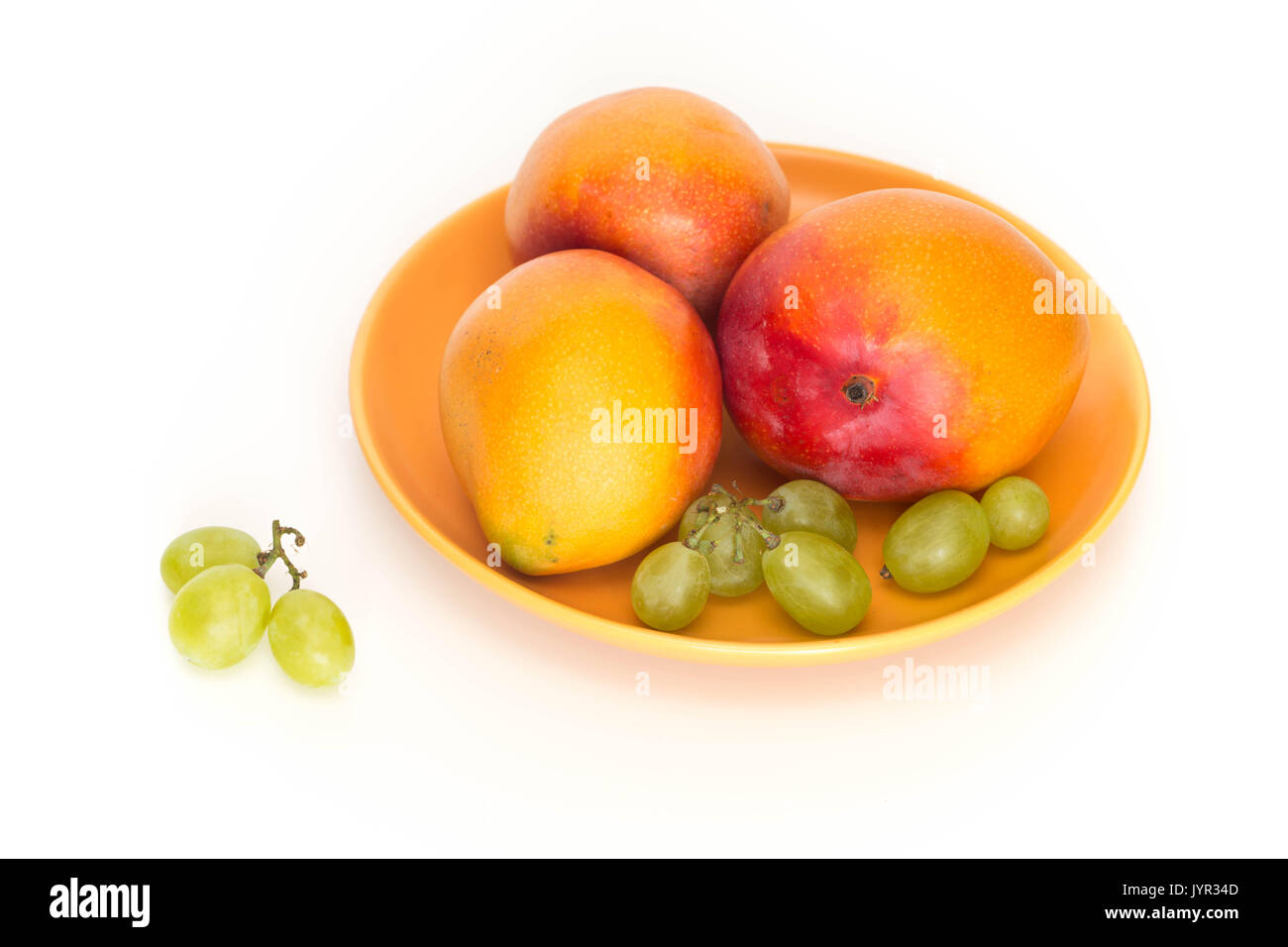 Fresh ripe mango and grape on the platter, shown on a light background ...