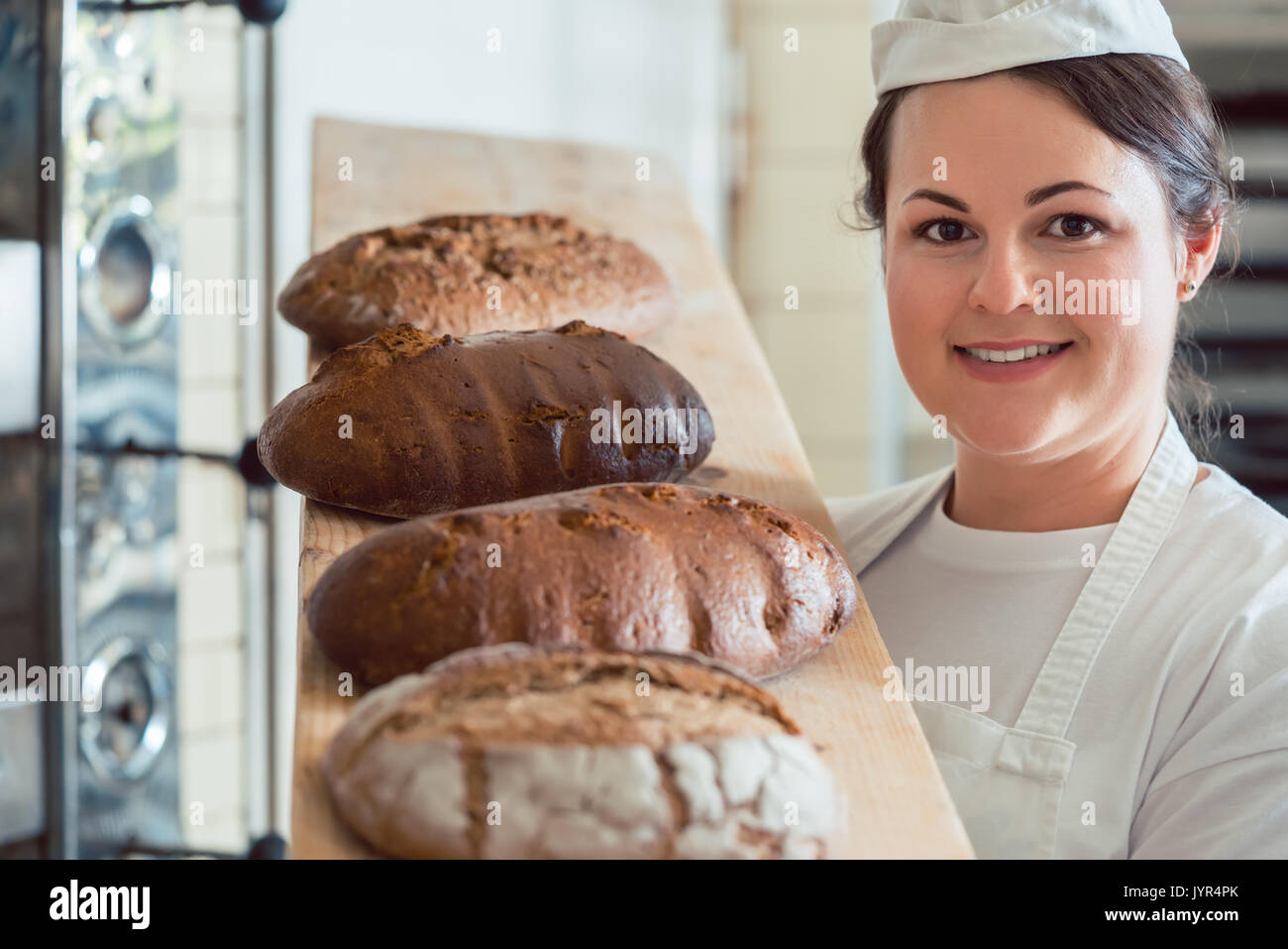 Baker woman presenting bread on board in bakery Stock Photo - Alamy