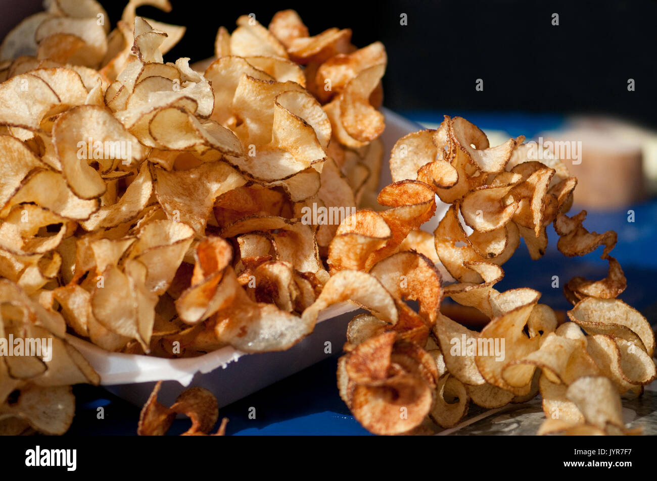 Freshly made hot curly potato chips overflowing onto blue tablecloth ...