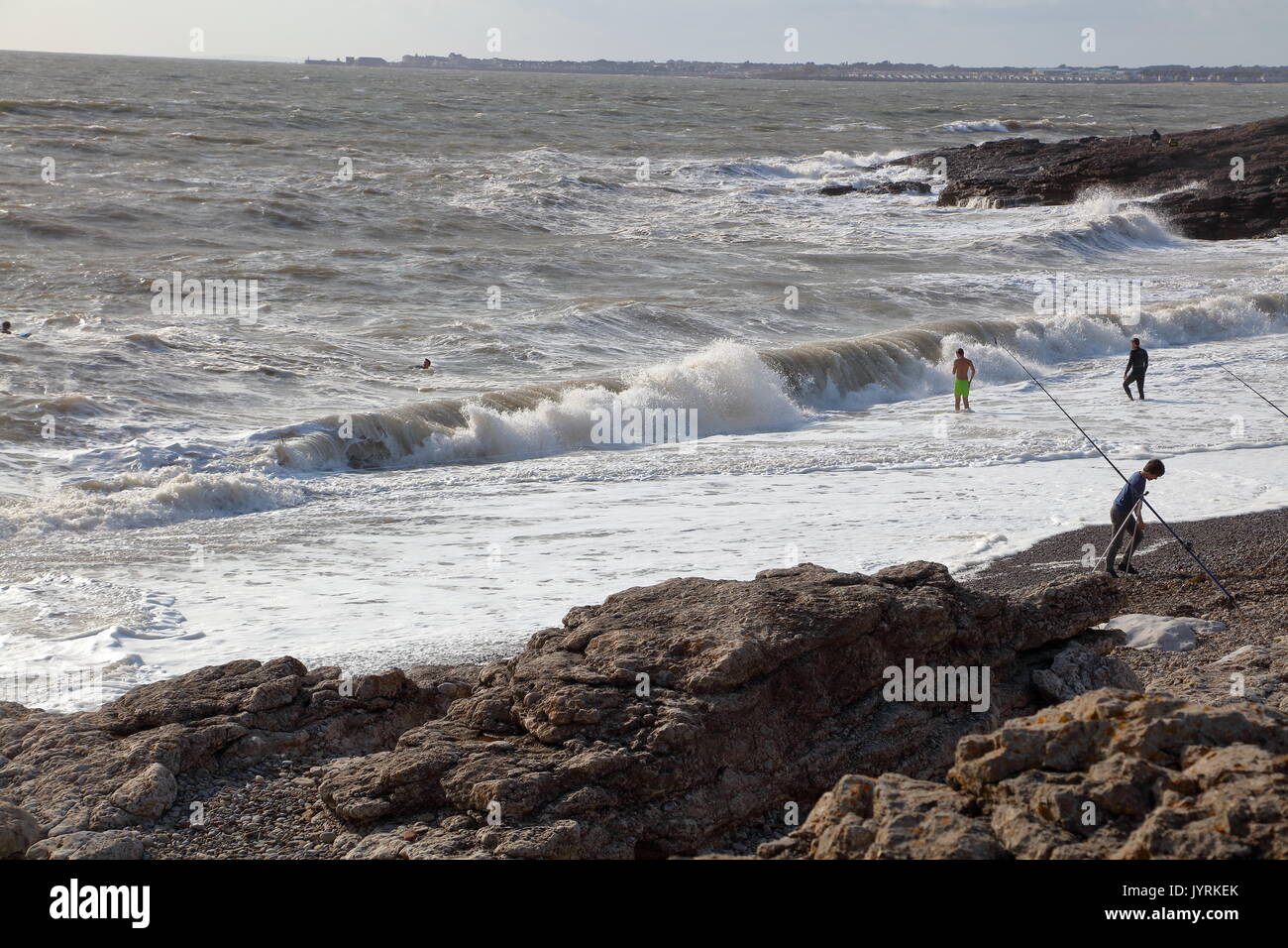 Anglers with rods fishing on a beach and swimmers riding the waves as ...