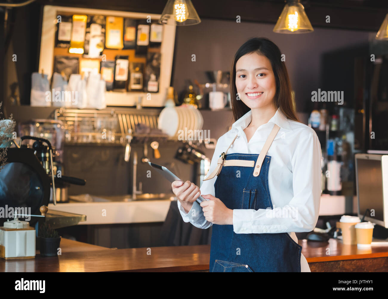 Asian female barista wear jean apron hold tablet computer coffee menu ...