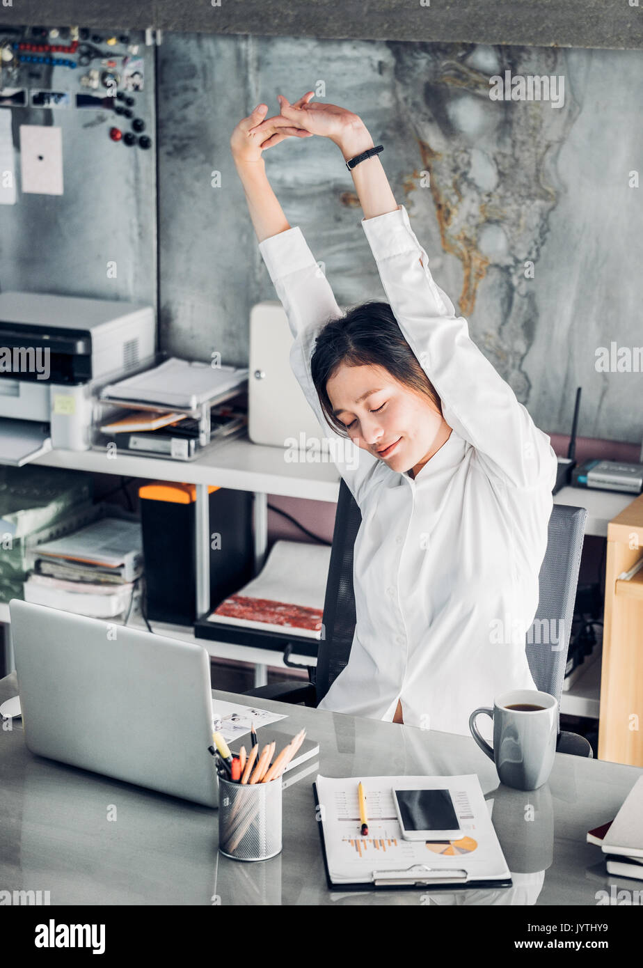 Asian businesswoman raise arm up stretching in front of desk from work ...