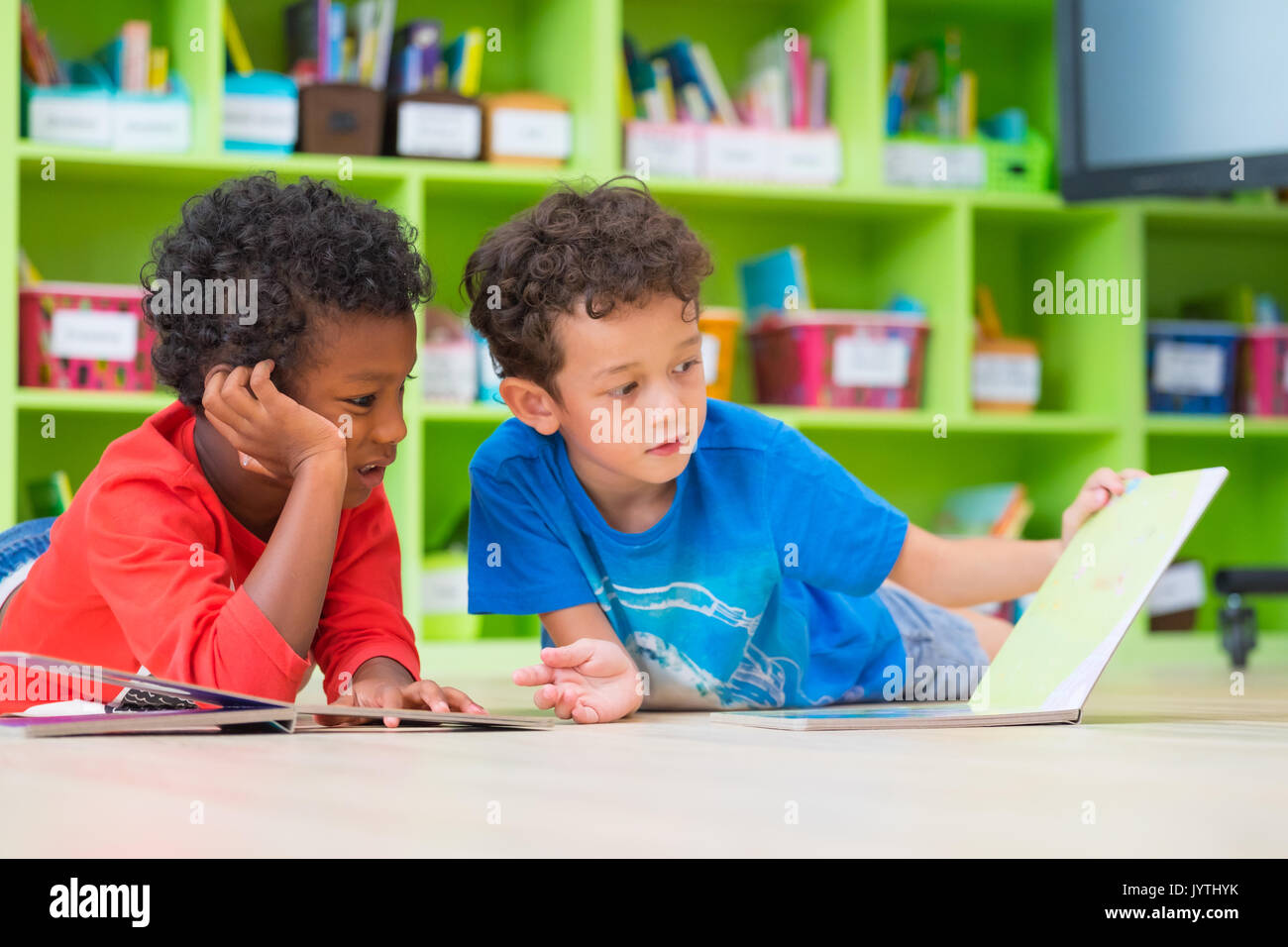 Two boy kid lay down on floor and reading tale book in preschool ...