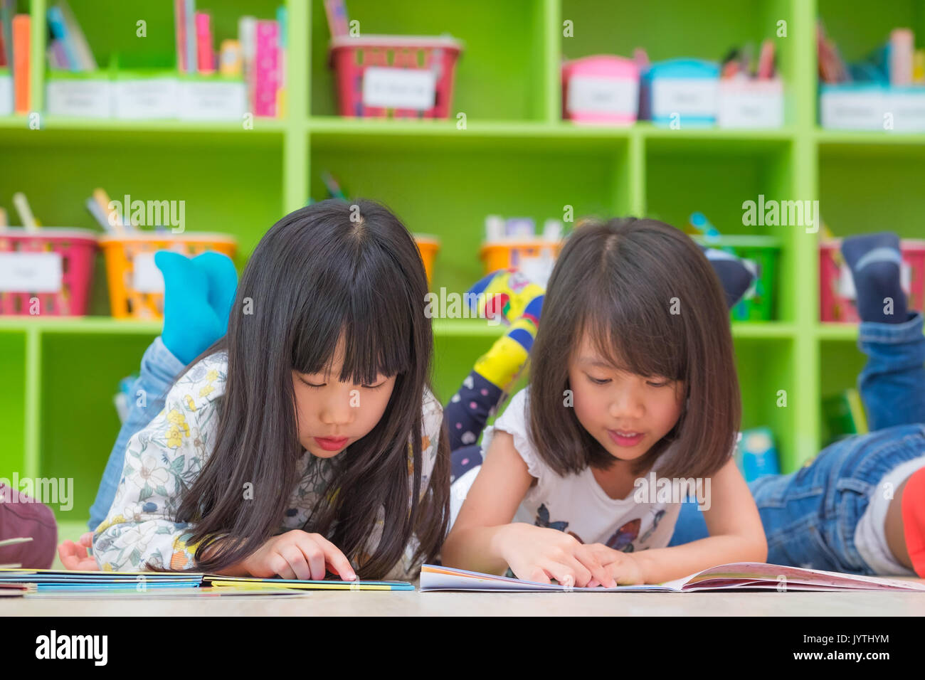 Two girl kid lay down on floor and reading tale book in preschool ...