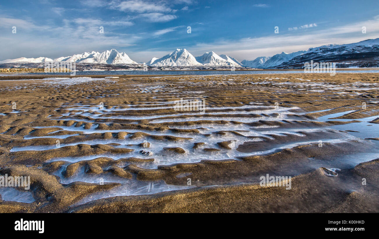 The icy sandy beach surrounding the snow capped mountains Breivikeidet ...