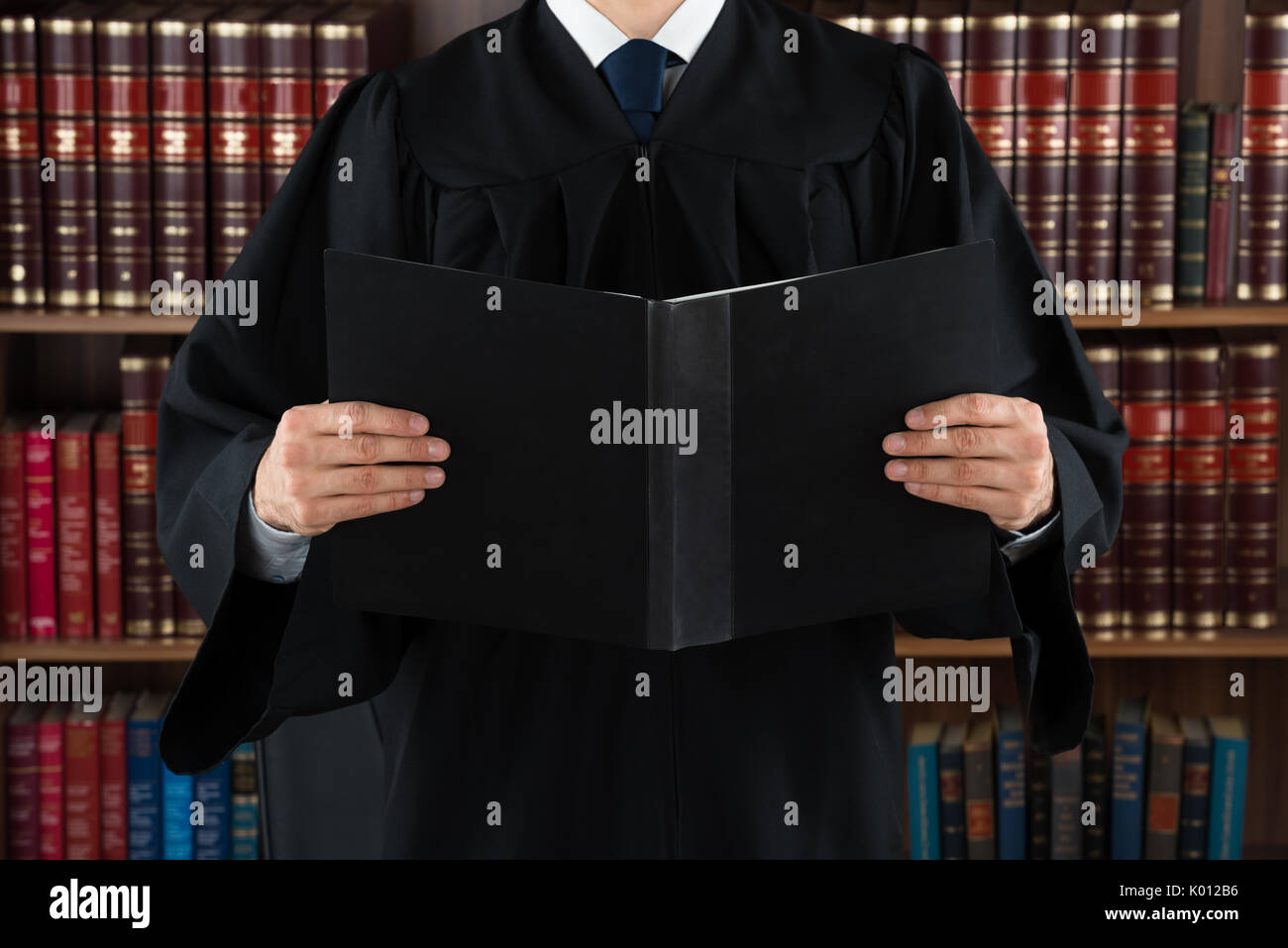 Midsection of judge holding legal book while standing against bookshelf ...