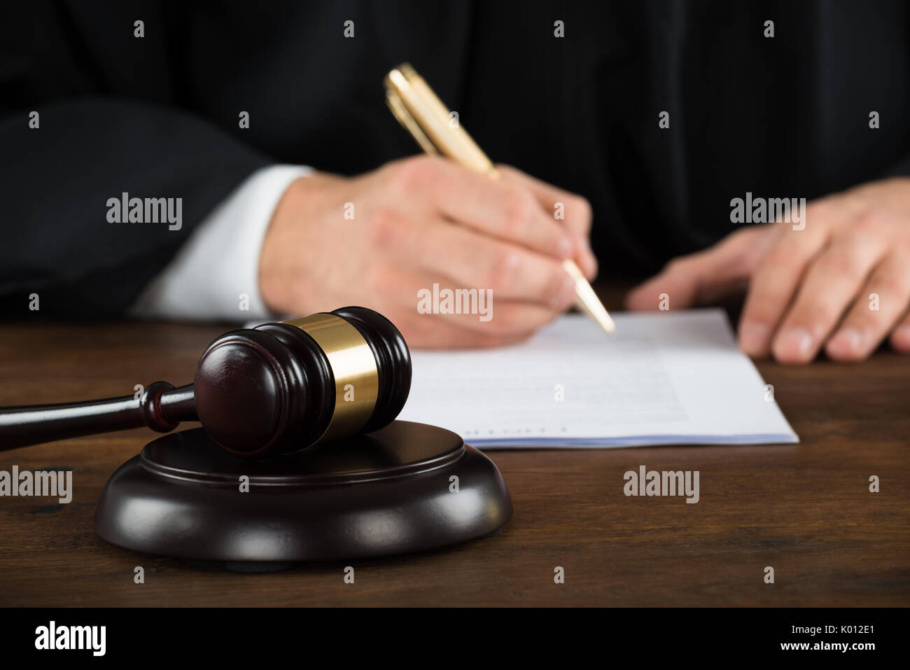 Midsection of male judge writing on legal documents at desk in ...