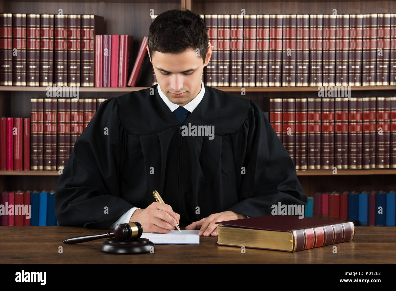 Young male judge making legal documents at desk against bookshelf in ...