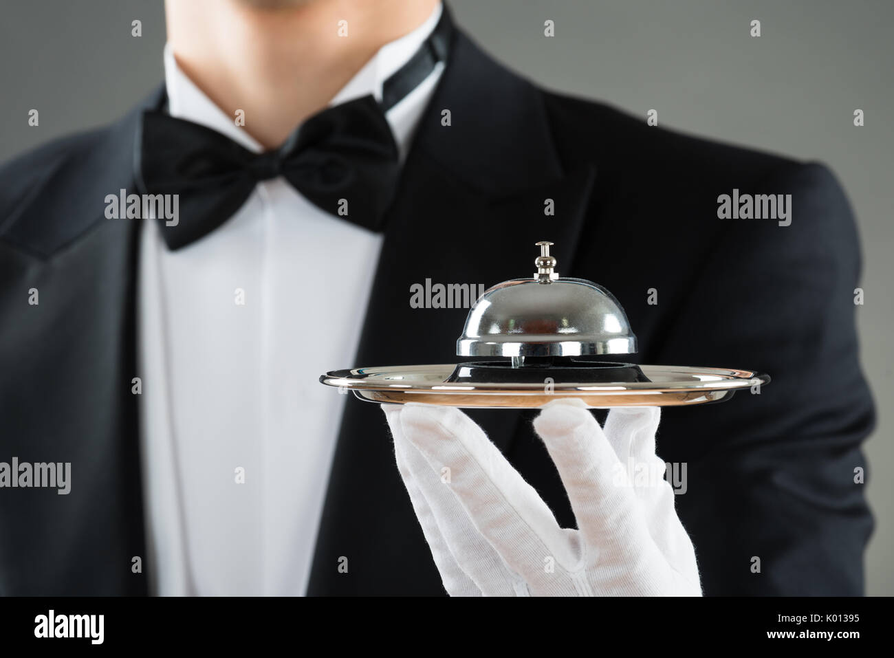 Midsection of waiter holding service bell in plate against gray ...