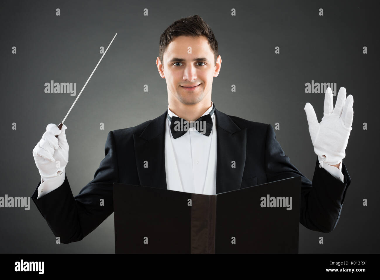 Portrait of smiling music conductor holding baton against gray ...